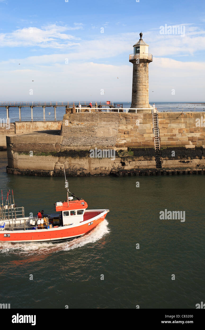 Fishing boat passing the lighthouse at the entry to Whitby harbour ...
