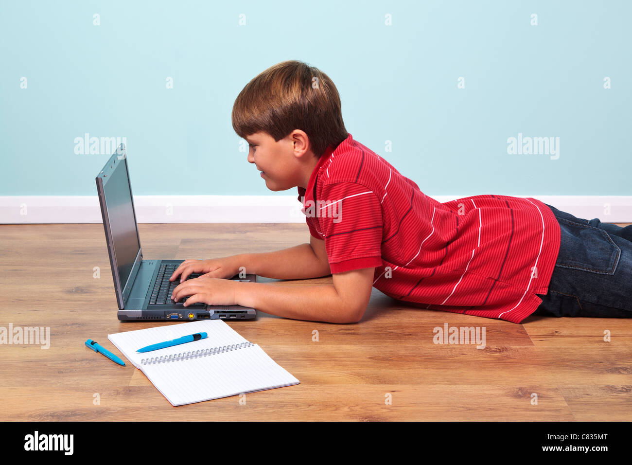 Photo of a boy lying on the floor typing on his laptop computer Stock ...