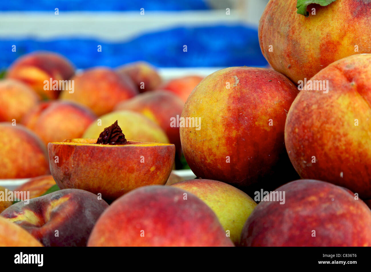 Ripe yellow peaches on display in a market with one cut in a half with ...