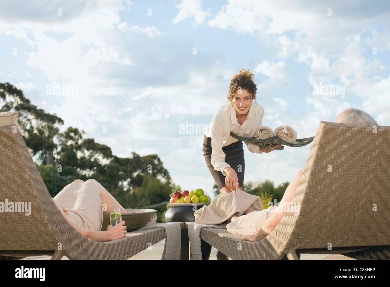 Waitress serving couple relaxing by pool Stock Photo - Alamy