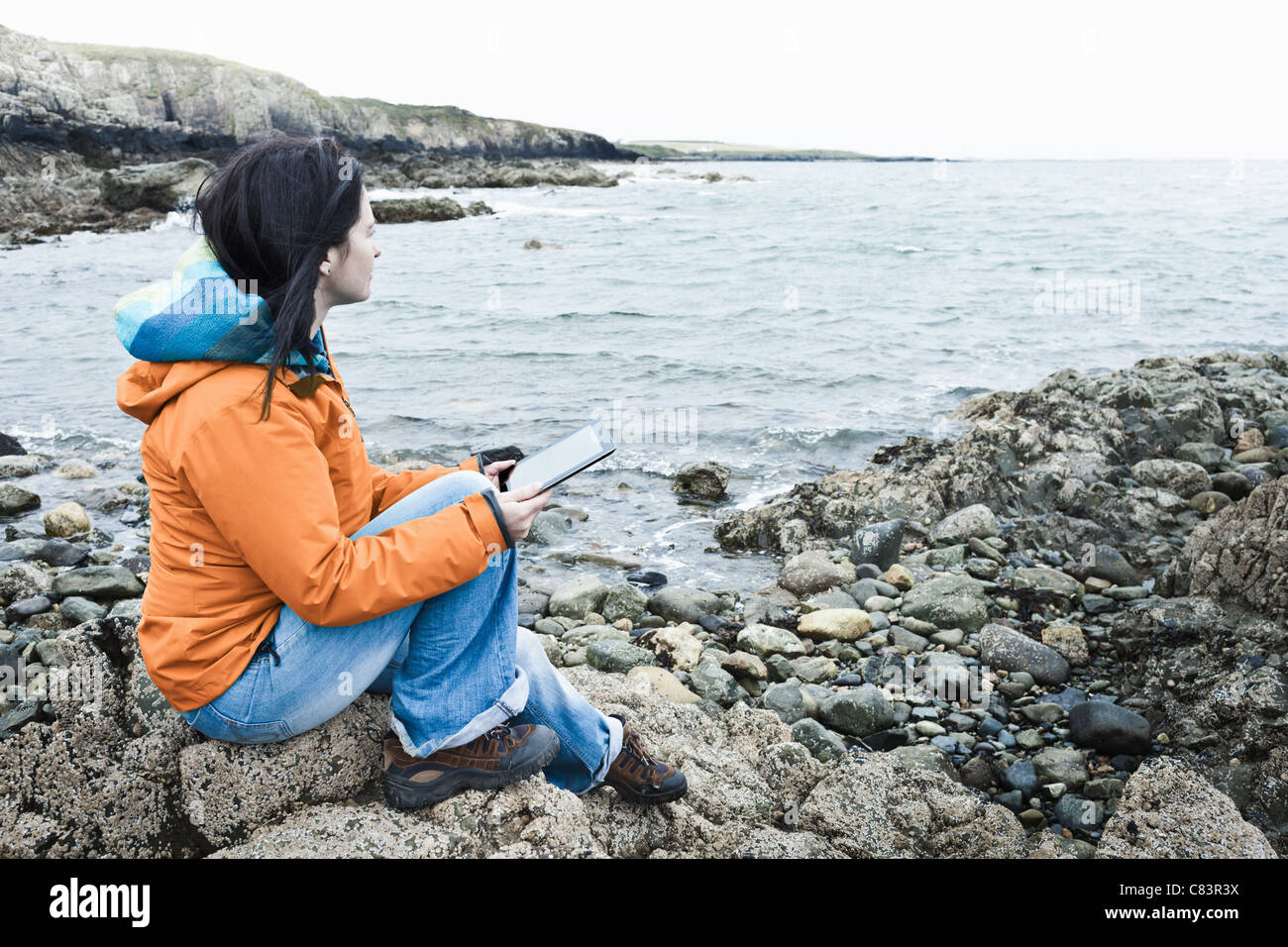 Woman reading on rocky beach Stock Photo - Alamy