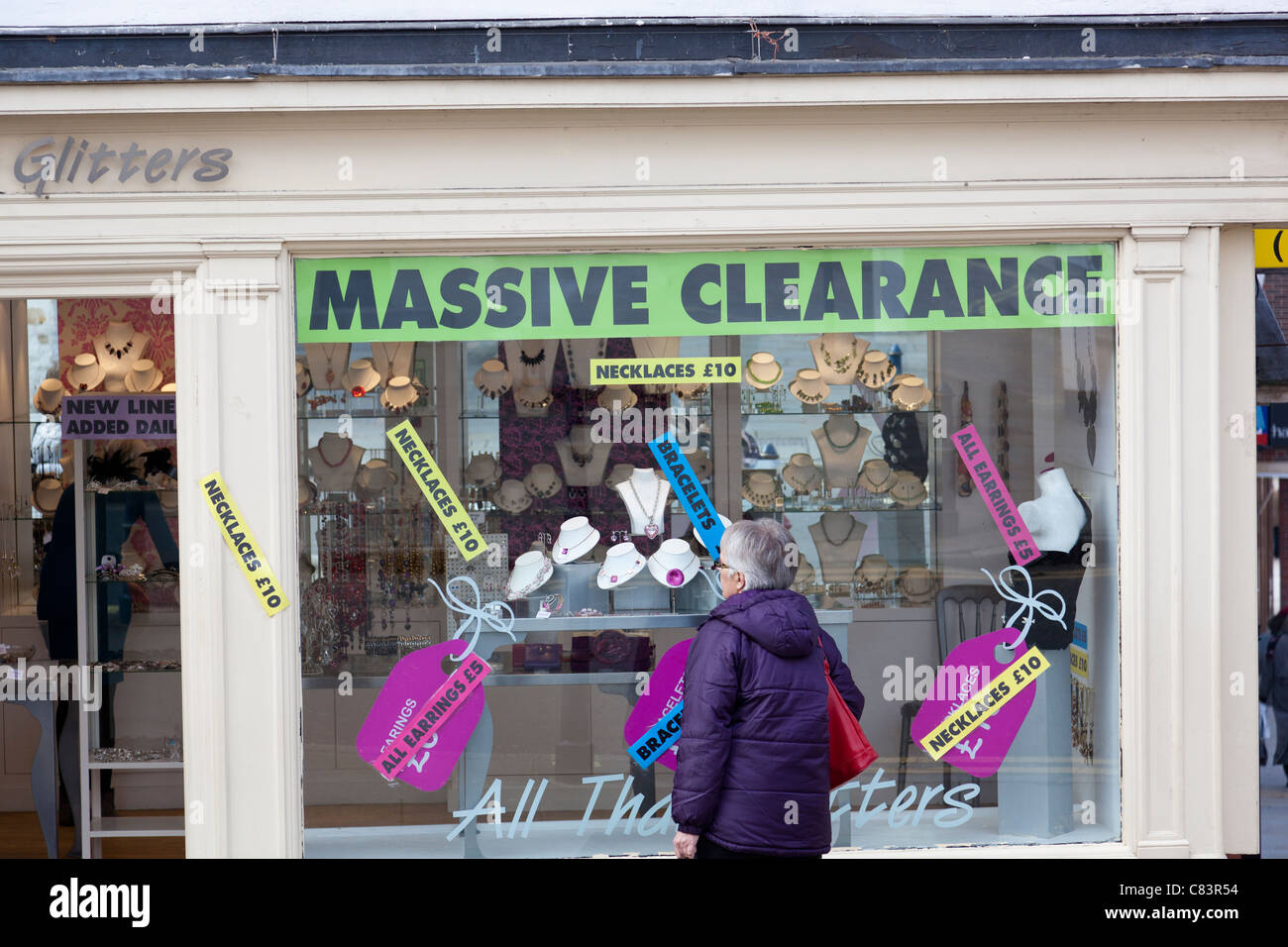 Woman looks at the window display of a jewellers with a large sale sign ...