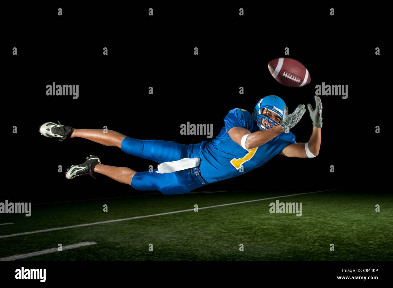 Mixed race football player jumping in mid-air catching football Stock ...