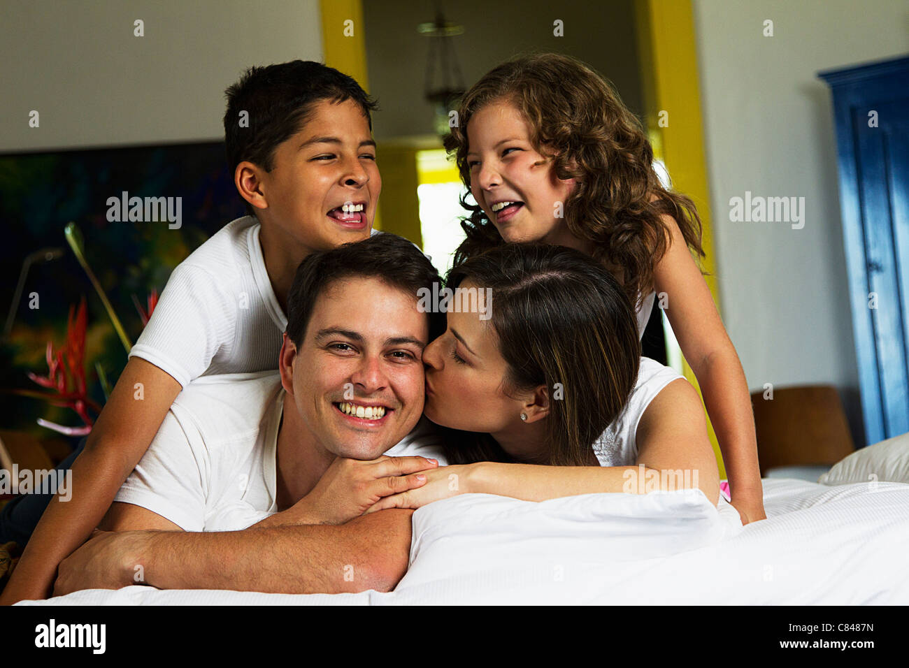Smiling Hispanic family laying on bed together Stock Photo - Alamy