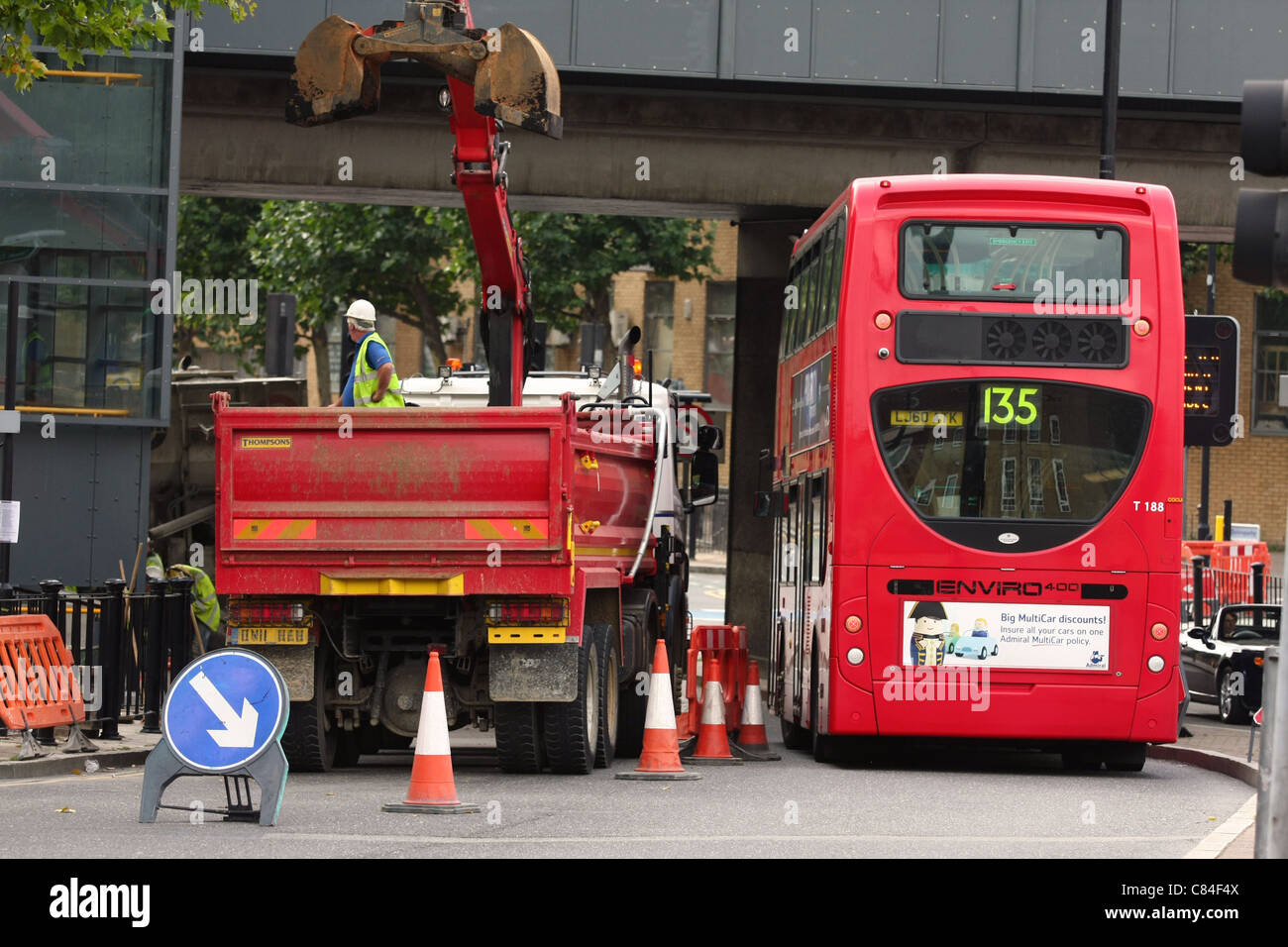 a bus passing a truck unloading material in a set of roadworks under a ...