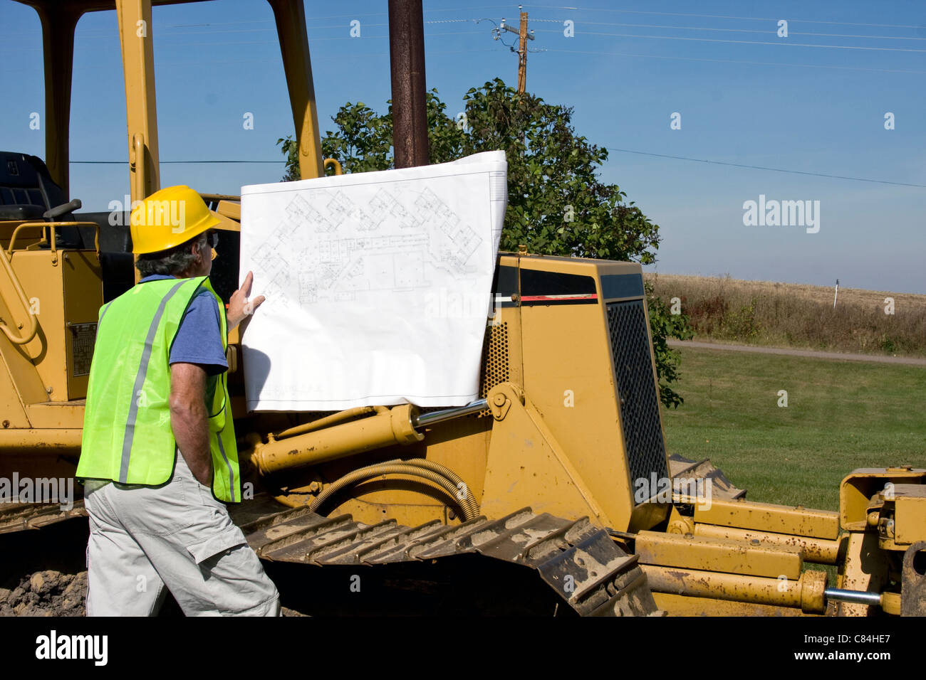 construction worker looking at blueprints with a bull dozer in the ...