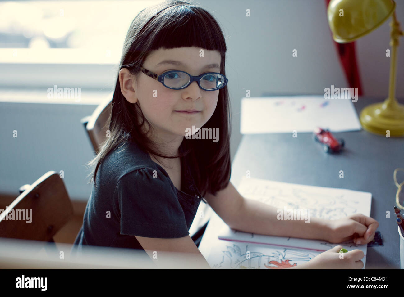 Girl sitting at desk with coloring book Stock Photo - Alamy