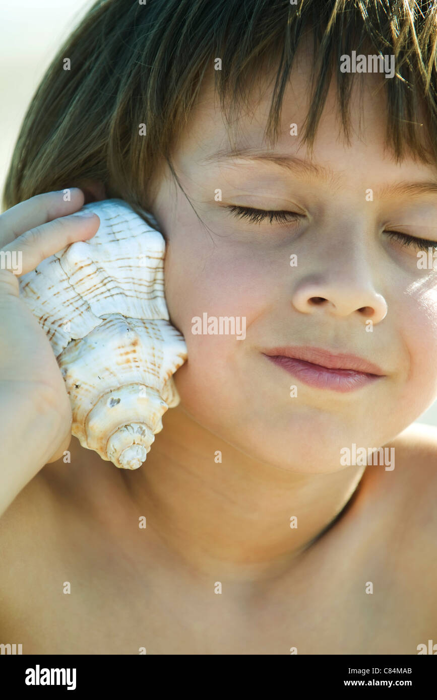 Boy listening to seashell with eyes closed Stock Photo - Alamy