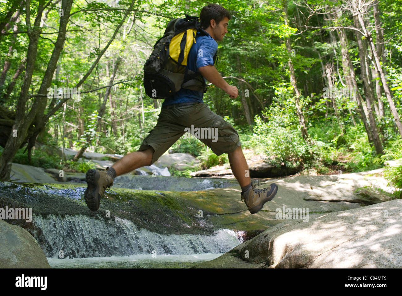 Man jumping over stream through woods Stock Photo - Alamy