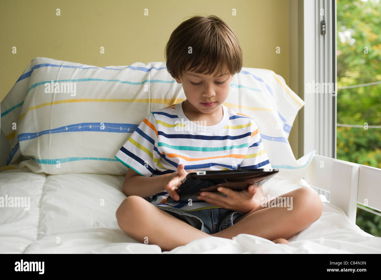 Boy sitting on bed, using digital tablet Stock Photo - Alamy
