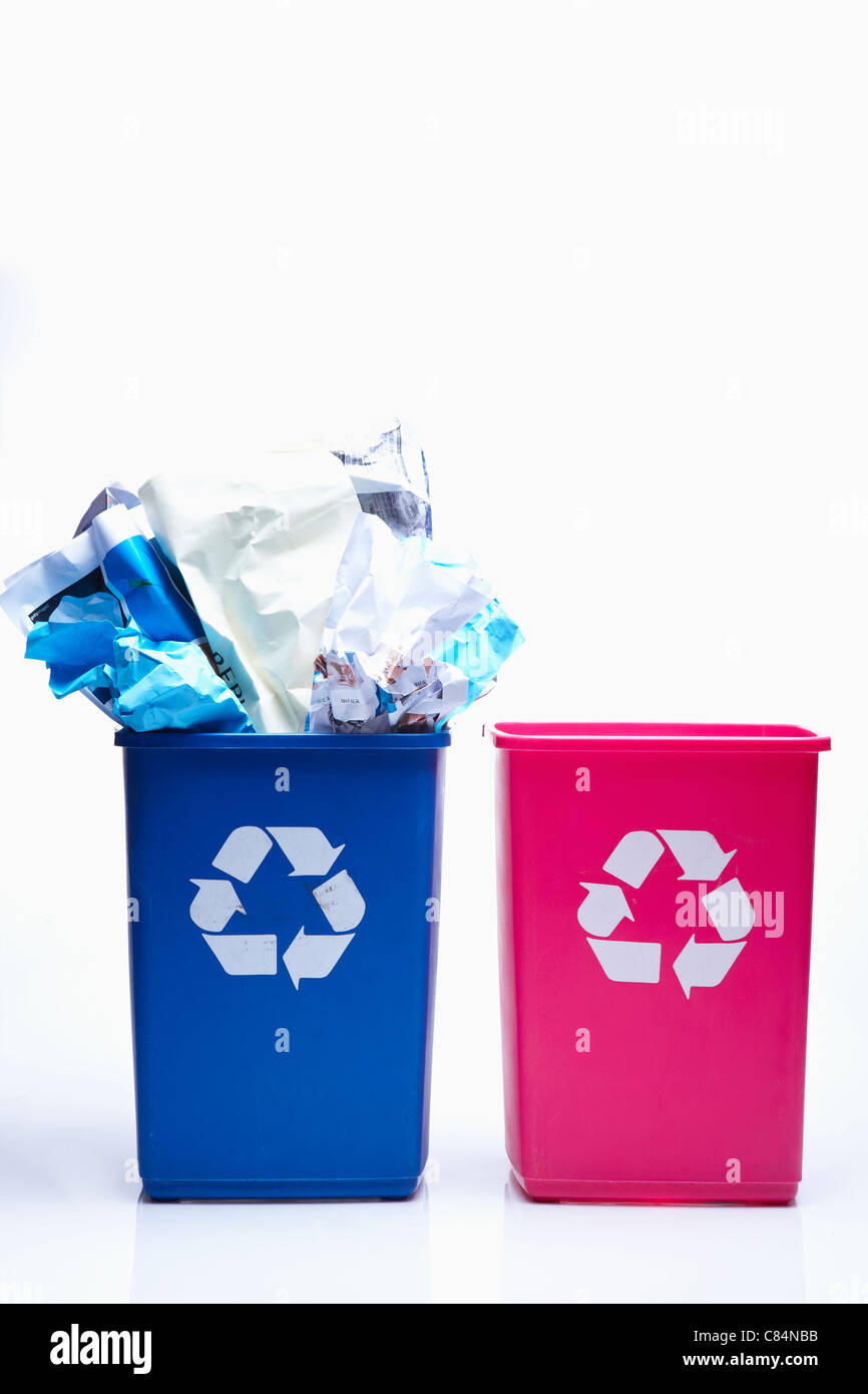 A blue trash basket full of paper trash and another red trash basket ...