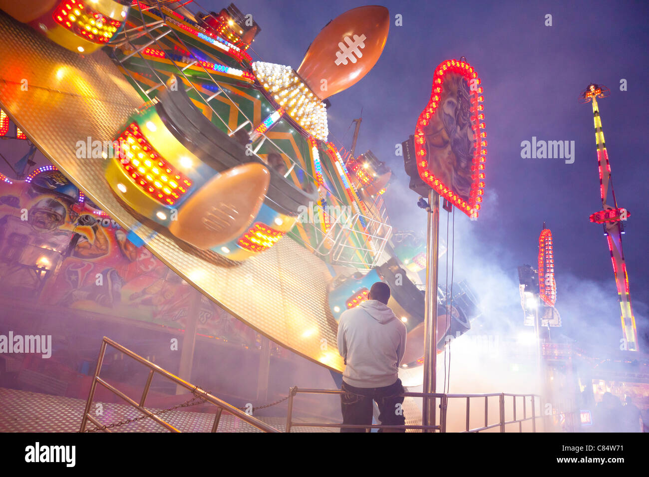 Fairground worker watching a carousel funfair ride at night at Goose ...