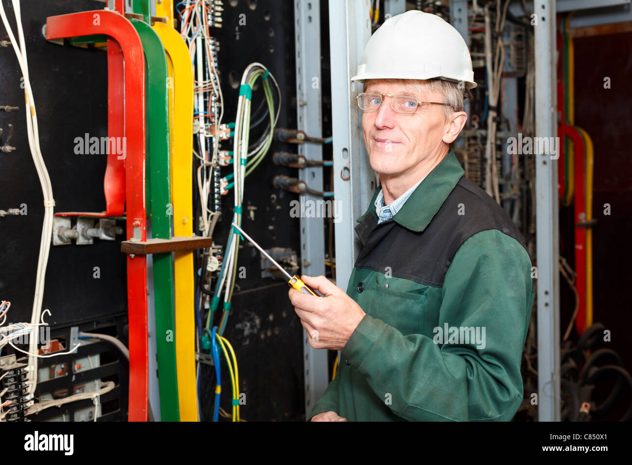Mature electrician working in white hard hat with cables and wires ...