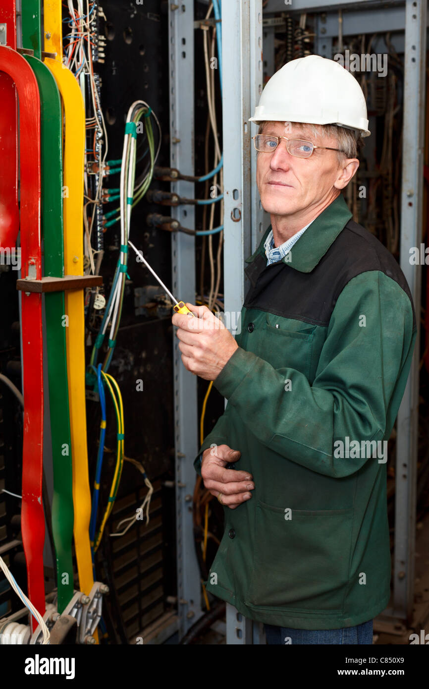 Mature electrician working in white hard hat with cables and wires ...