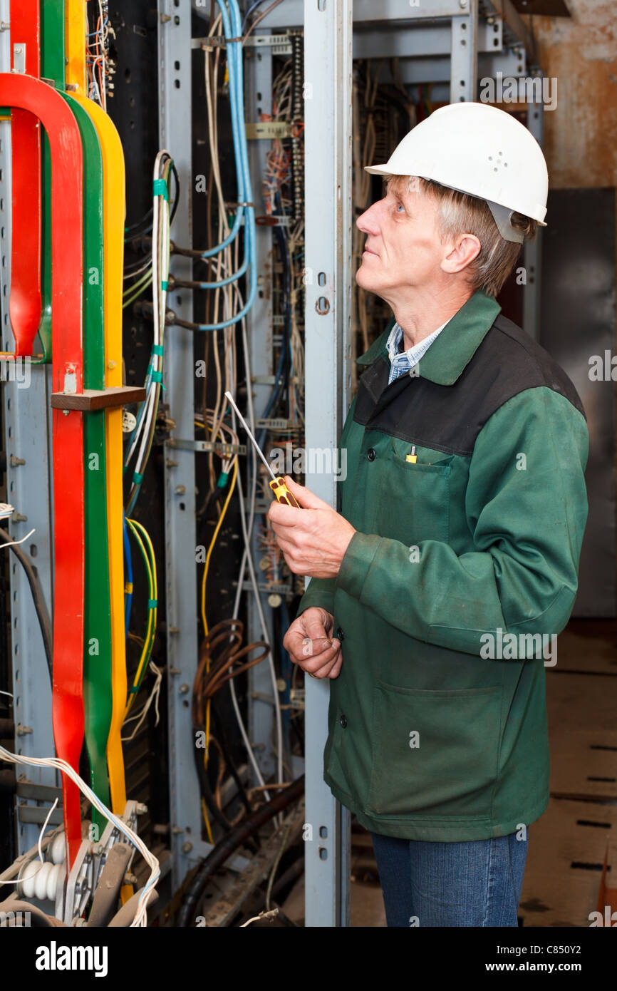 Mature electrician working in white hard hat with cables and wires ...