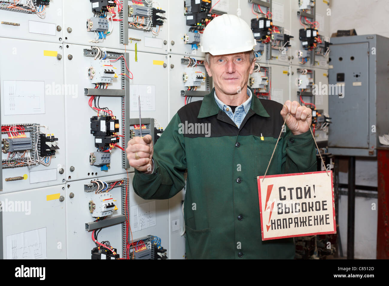 Mature electrician working in white hard hat with cables and wires ...