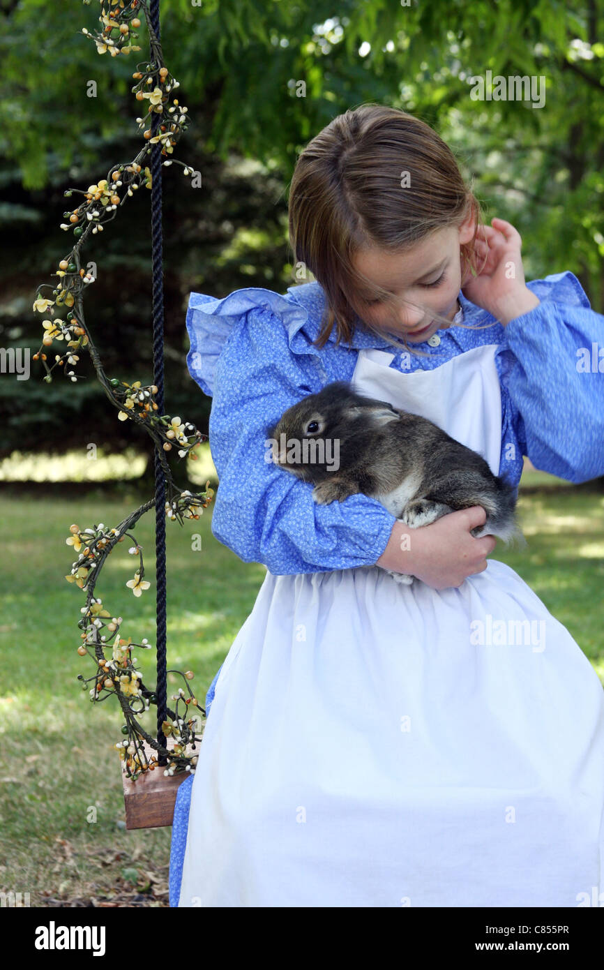 A young girl on a swing with a bunny pulling hair behind her wings ...