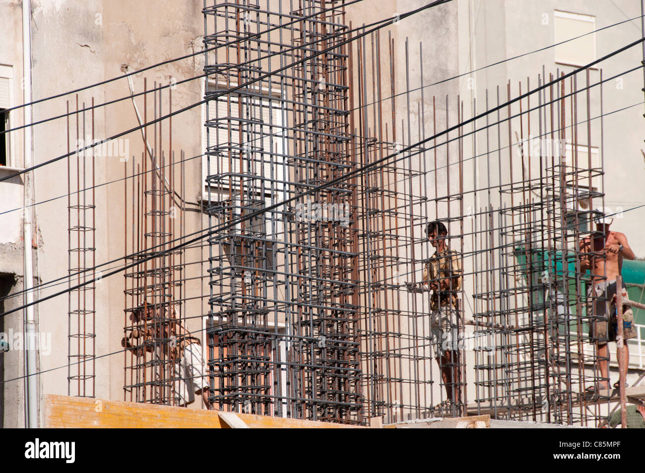 Three men working on a construction site putting metal rods together ...