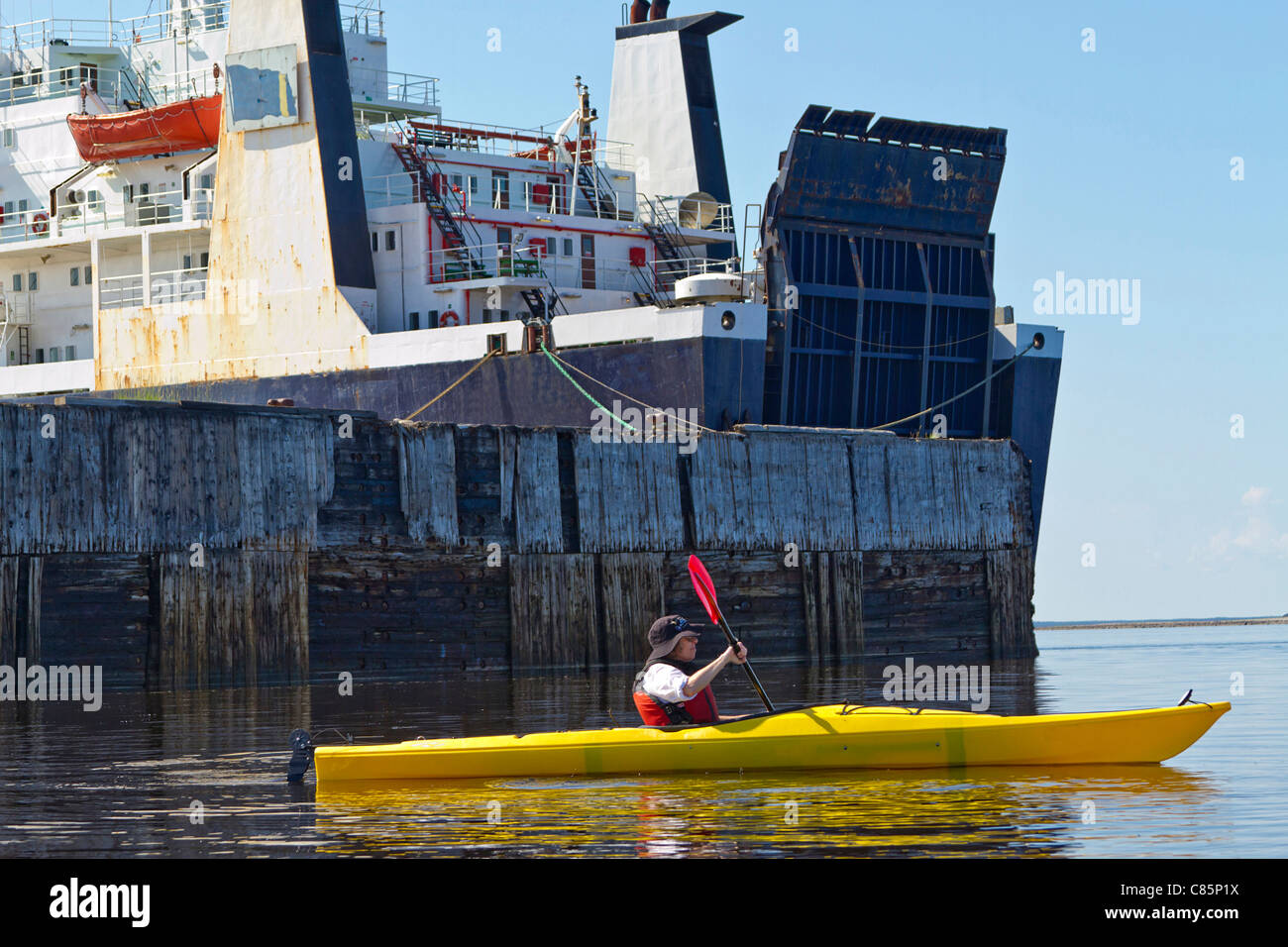 Woman kayaks past dock and cargo ship waiting to be loaded with grain ...