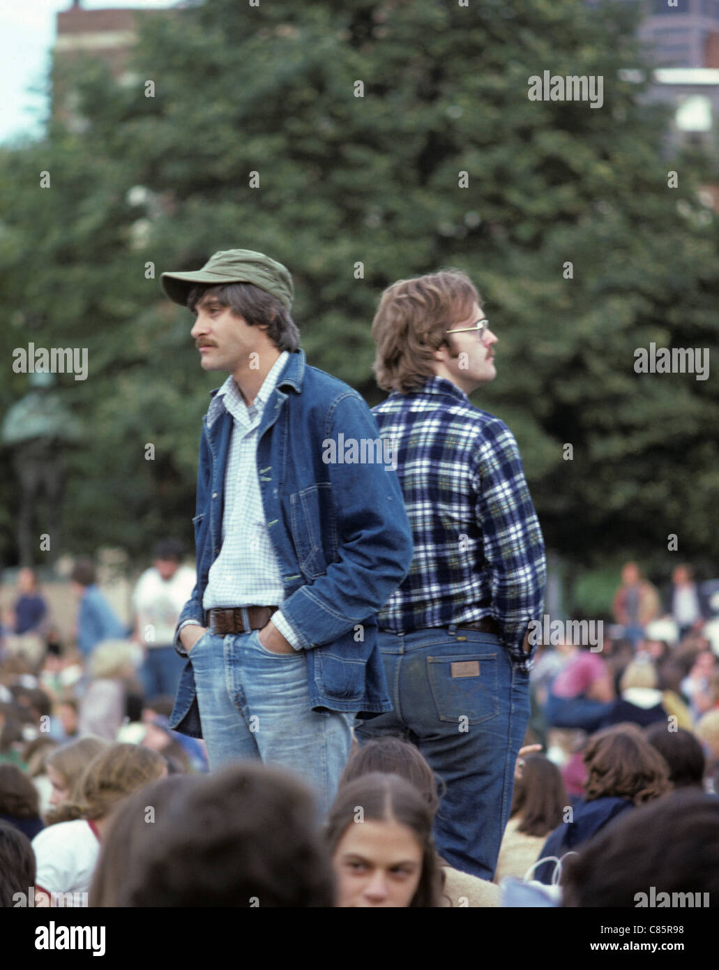 two young men stand back to back at festival watching rock group ...