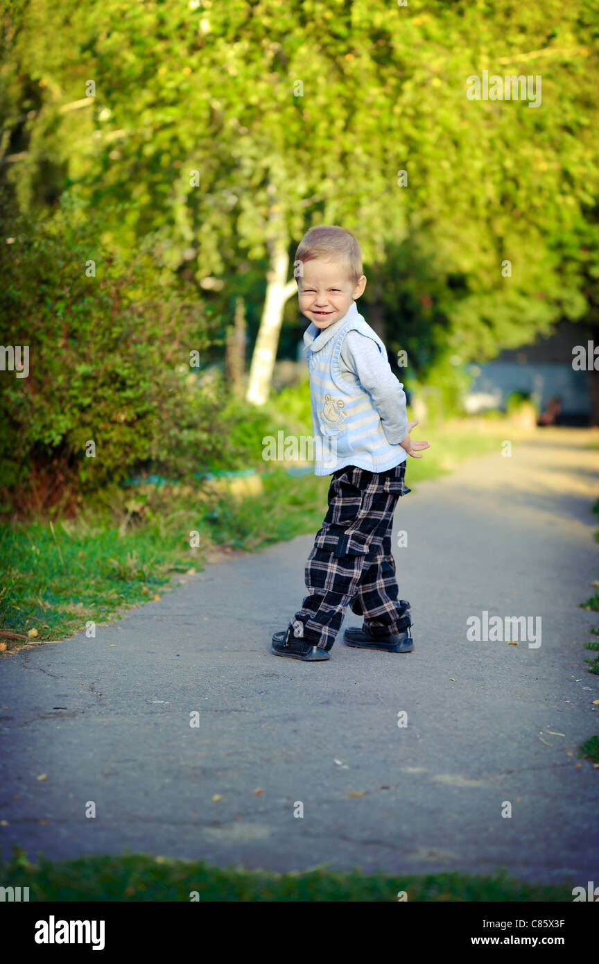 The child on avenue in the summer among green trees and bushes on the ...