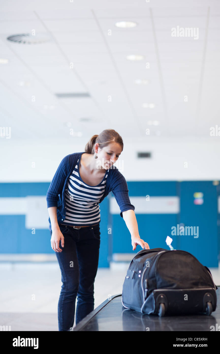 Baggage claim at the airport - pretty young woman taking her suitcase ...