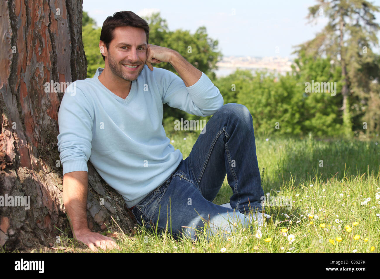 Man sitting against tree Stock Photo - Alamy