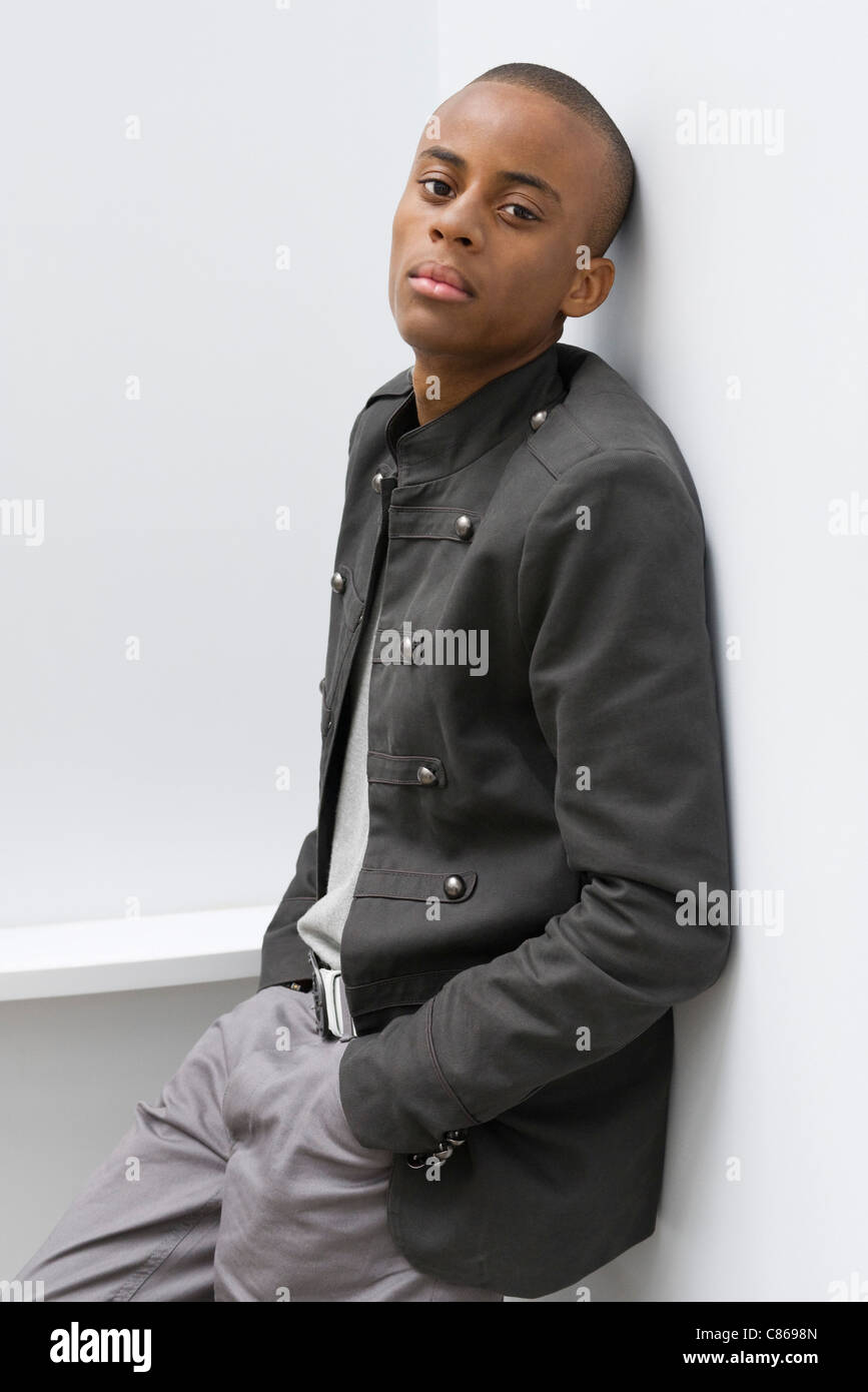 Young man leaning against wall with hands in pockets, portrait Stock ...