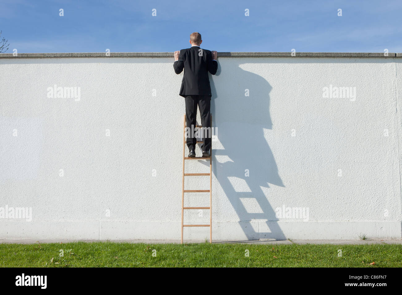 Businessman on ladder looking over wall Stock Photo - Alamy