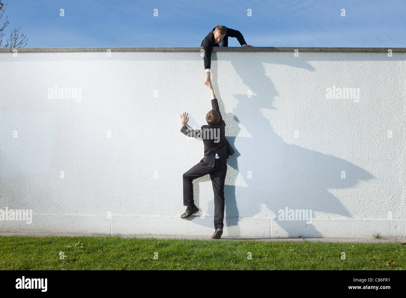 Businessman pulling colleague over wall Stock Photo - Alamy
