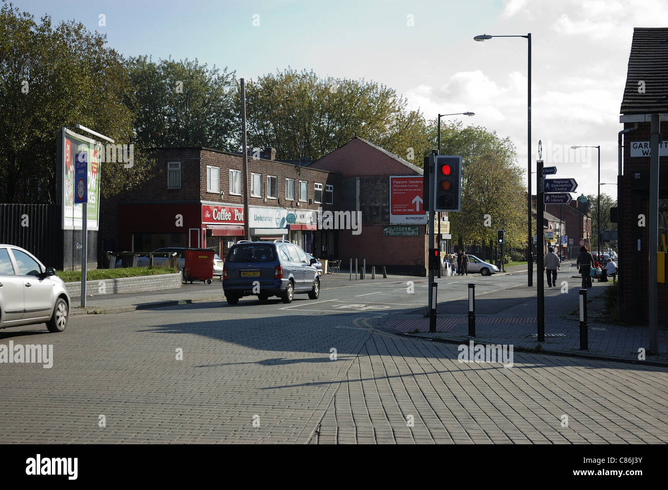 Road at junction with traffic and shops on left Stock Photo - Alamy