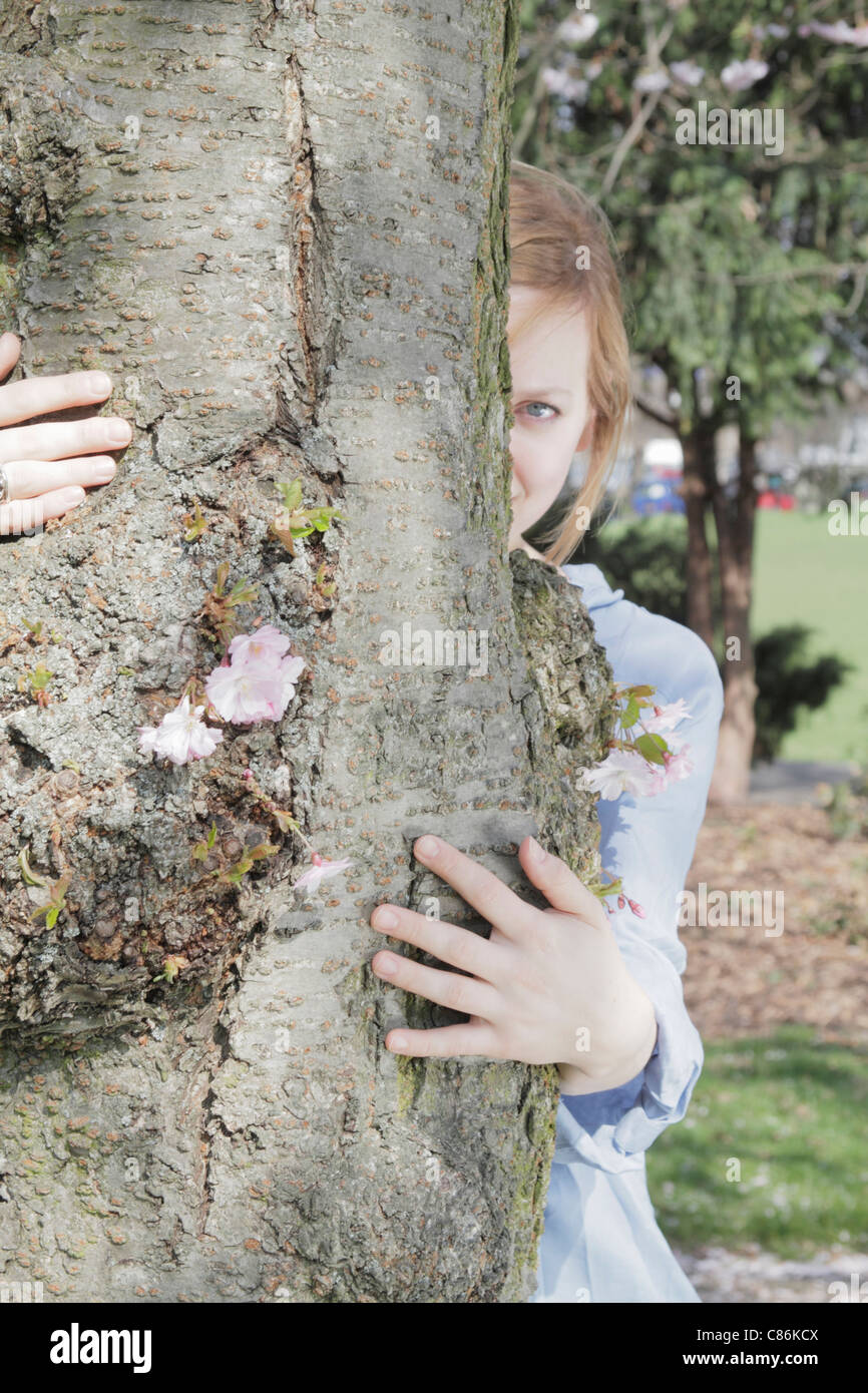 Woman peeking out from behind tree Stock Photo - Alamy