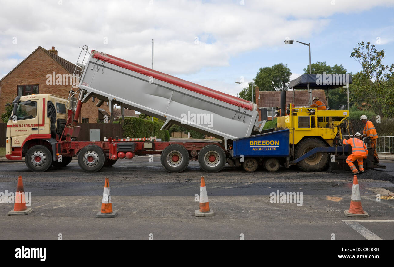 A lorry tipping a fresh delivery of asphalt into a tarmac machine ready ...