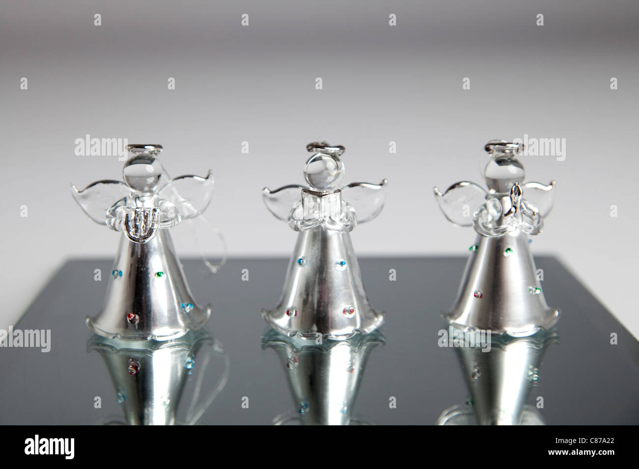 Three glass angels placed on a mirror plate, giving an abstract ...