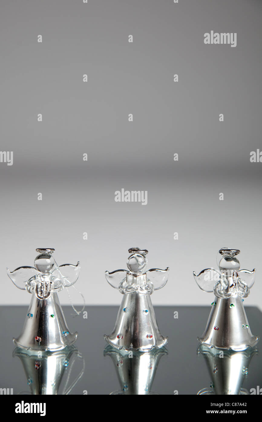 Three glass angels placed on a mirror plate, giving an abstract ...