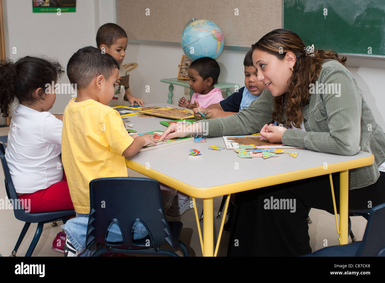 Preschool teacher helping 4 year old students put together a puzzle in ...