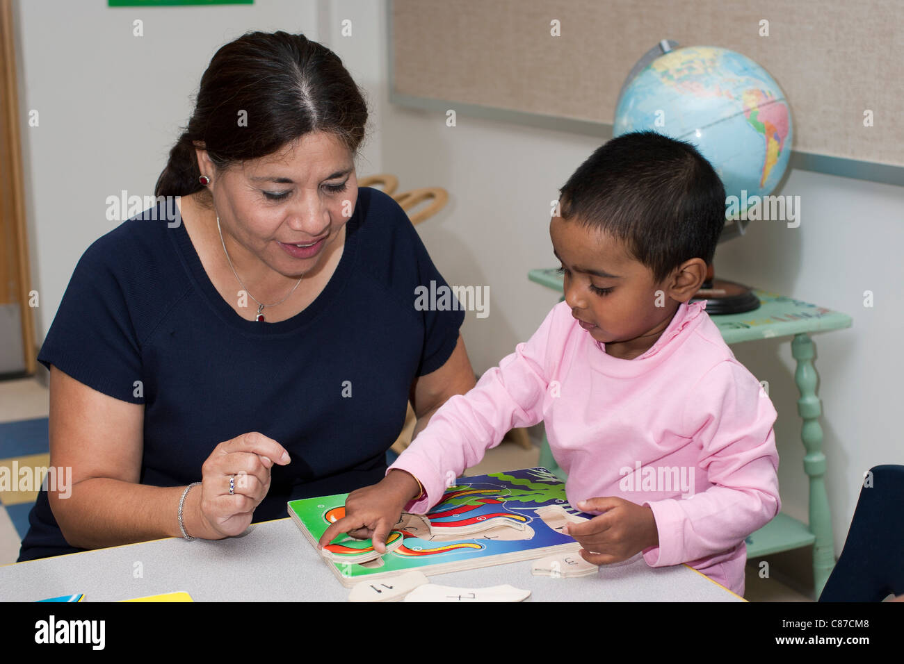 Preschool teacher helping 4 year old girl student put together a puzzle ...