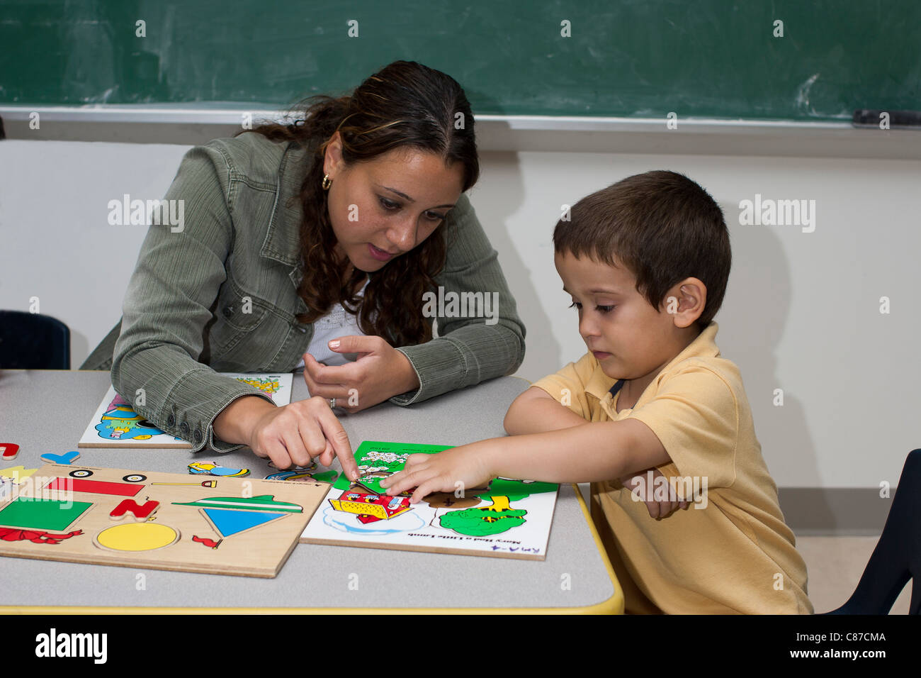 Preschool teacher helping 4 year old Caucasian boy student put together ...