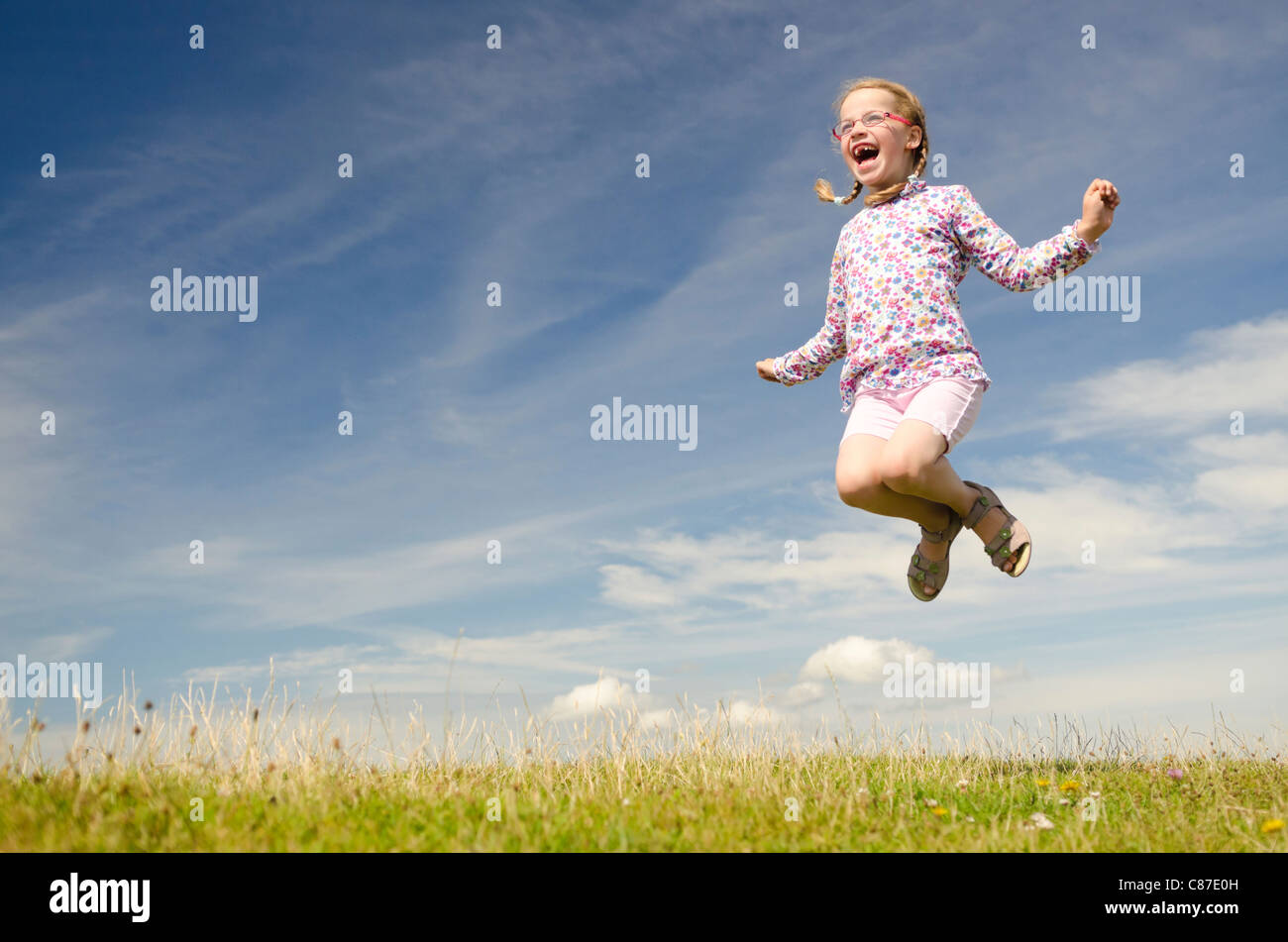 Happy little girl jumping in front of blue sky Stock Photo - Alamy