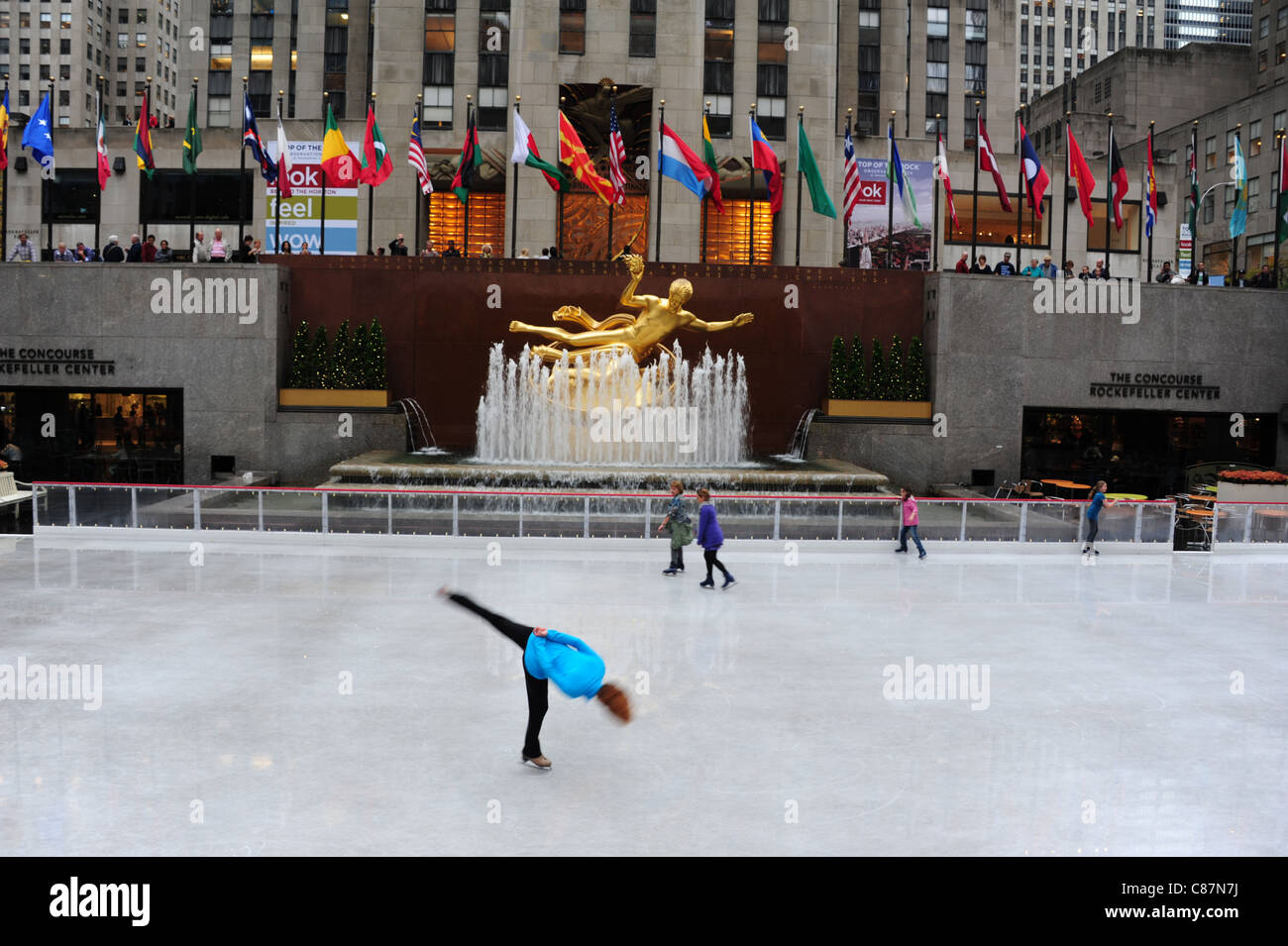 Female ice-skater moving one leg front gold Prometheus sculpture, flags ...