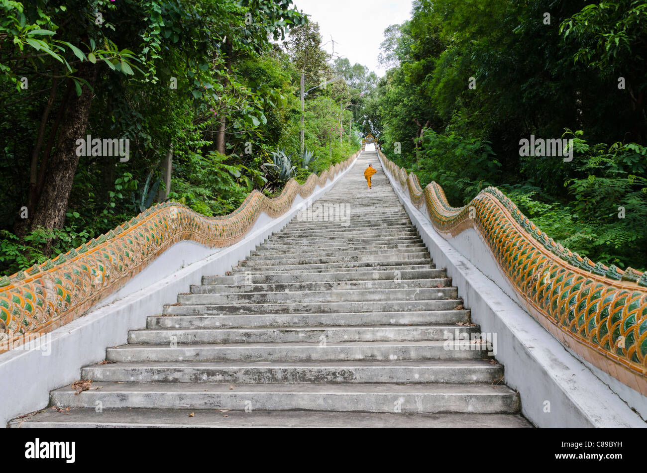 Novice monk in golden robe hikes up an extremely long staircase up a ...