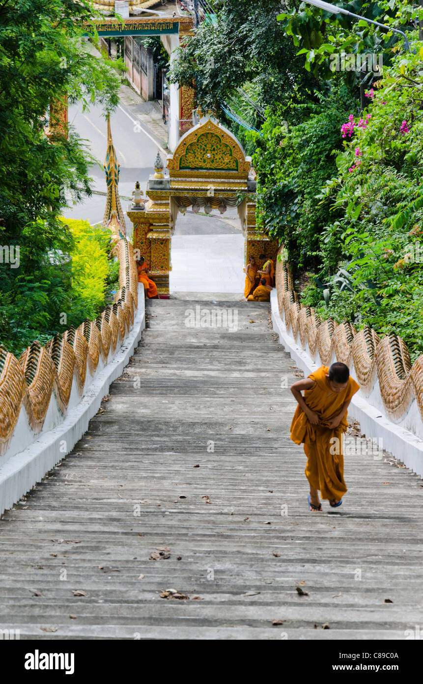 Novice monk in golden robe hikes up an extremely long staircase up a ...