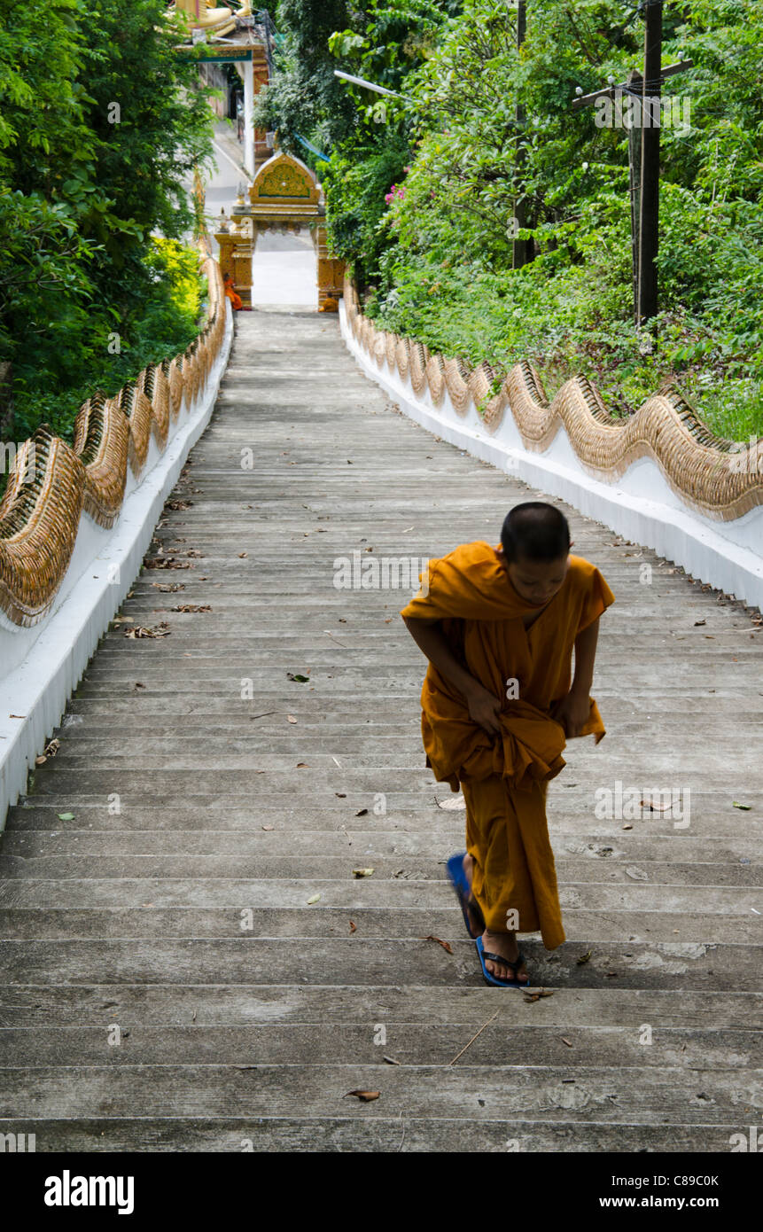 Novice monk in golden robe hikes up an extremely long staircase up a ...