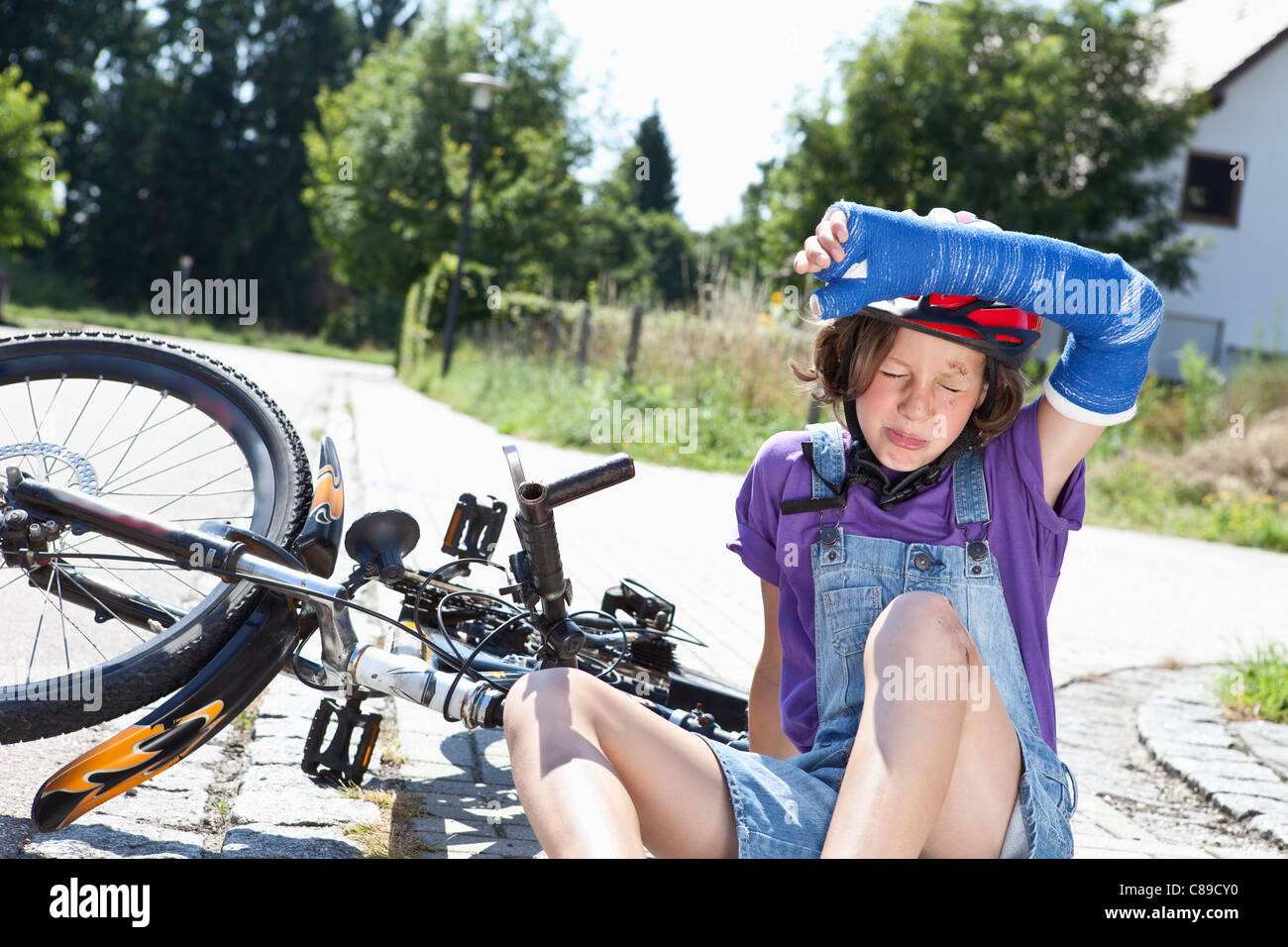 Germany, Bavaria, Wounded girl sitting on road after bicycle accident ...