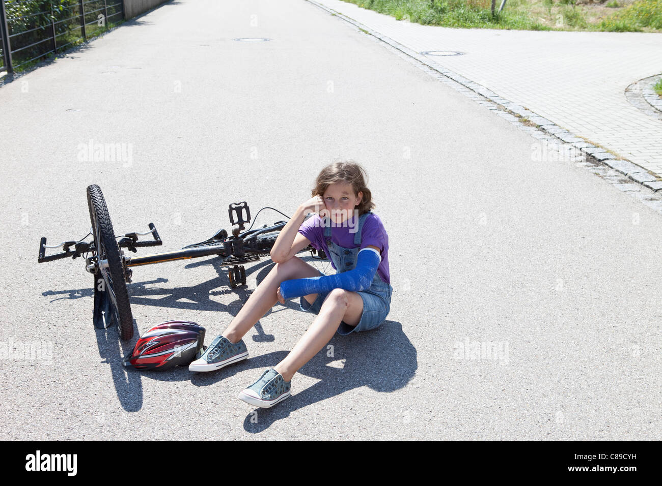Germany, Bavaria, Wounded girl sitting on road after bicycle accident ...