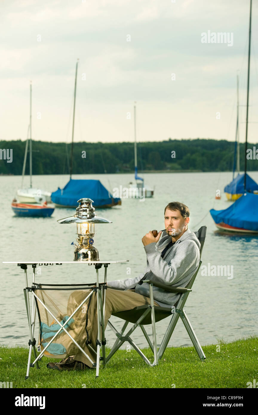 Germany, Bavaria, Woerthsee, Man smoking pipe near lakeshore while ...