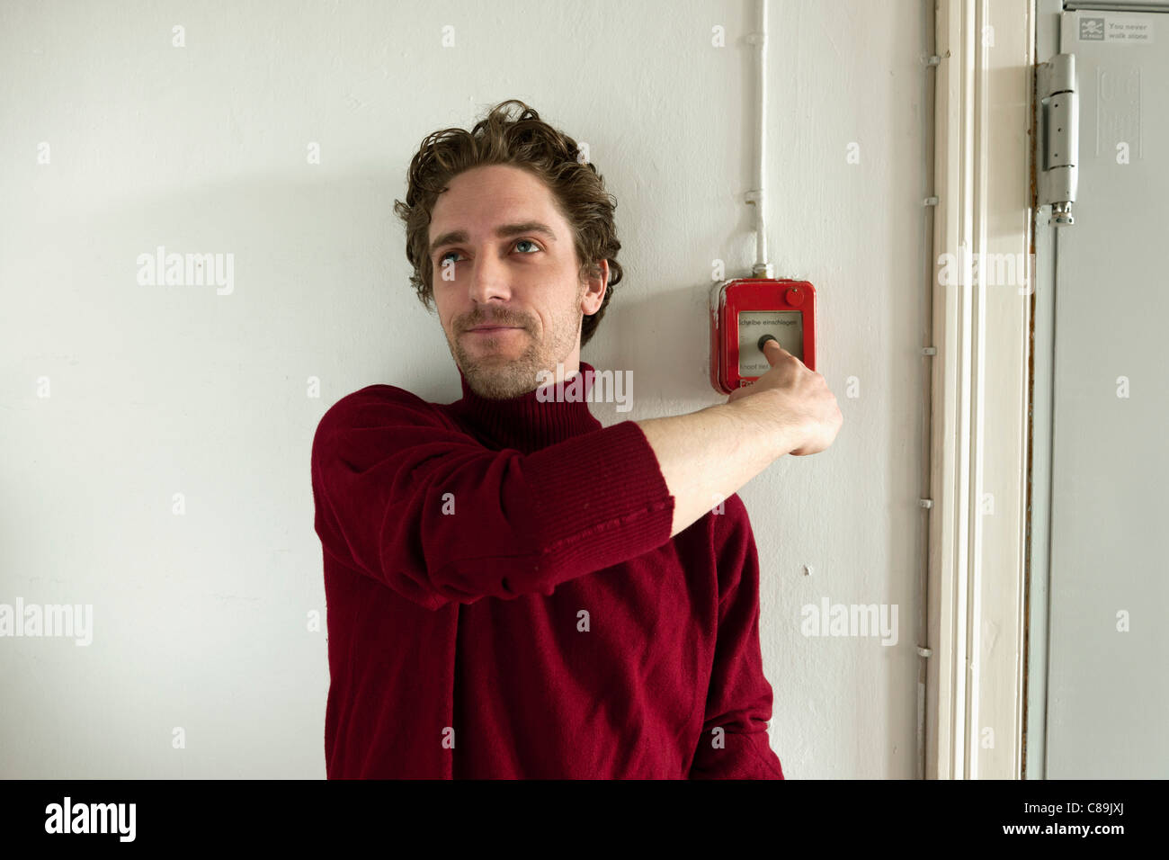 Mid adult man leaning on wall and pressing fire alarm Stock Photo - Alamy