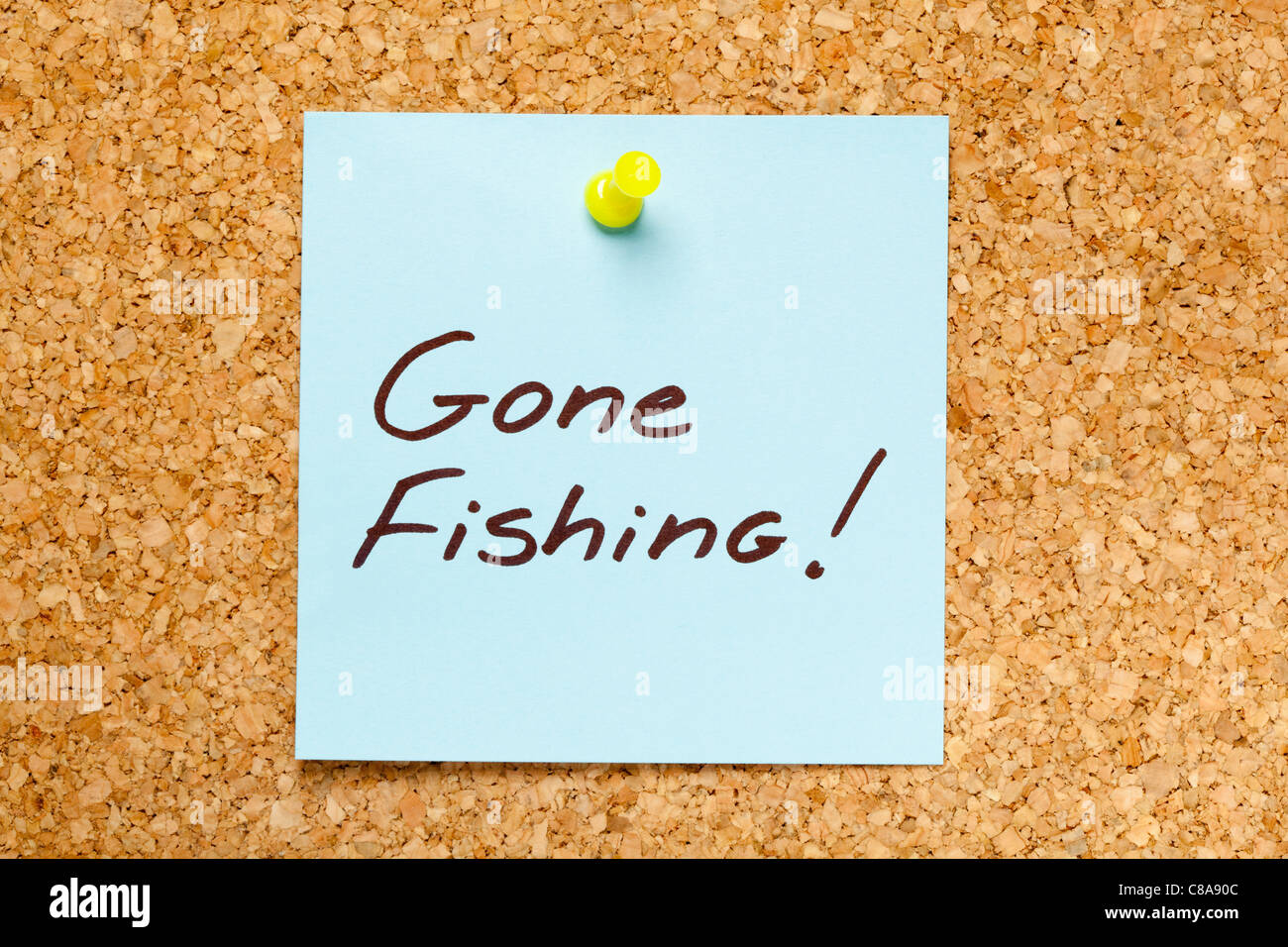 GONE FISHING! written on a blue sticky note on an office cork bulletin ...