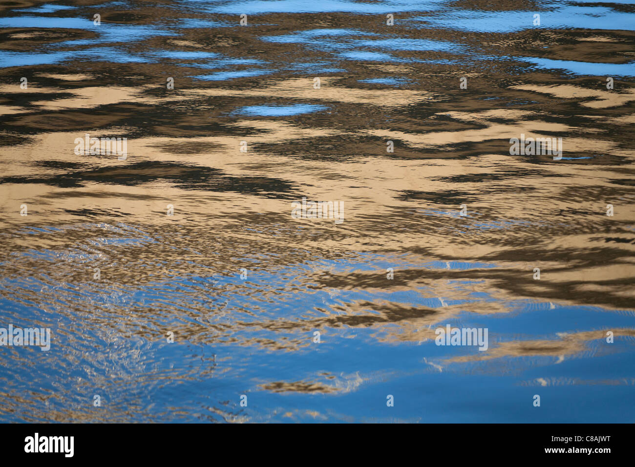 Reflections in moving river water creating abstract patterns in browns ...
