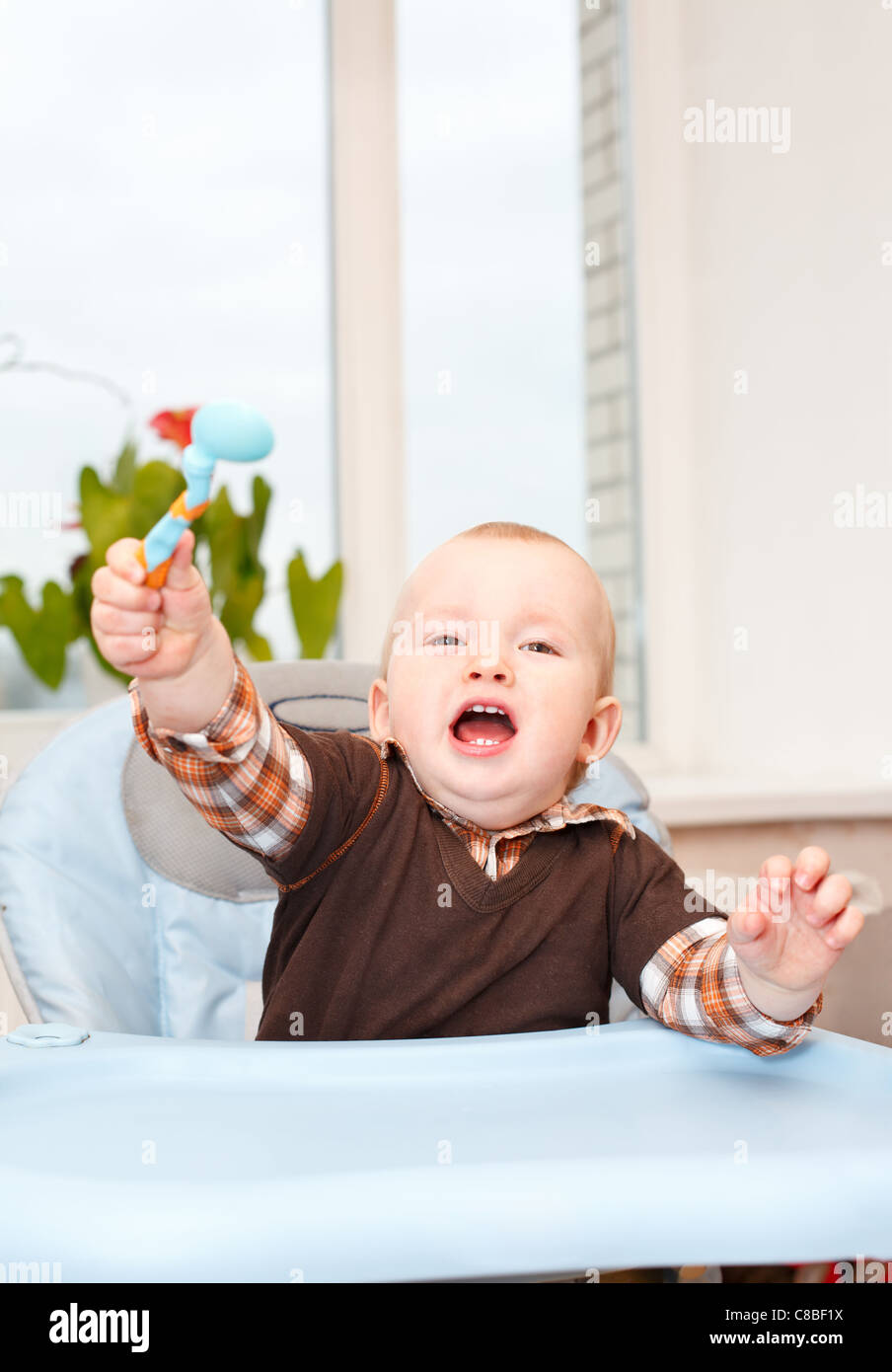 Little kid sitting in highchair and waving his spoon. Expression during ...